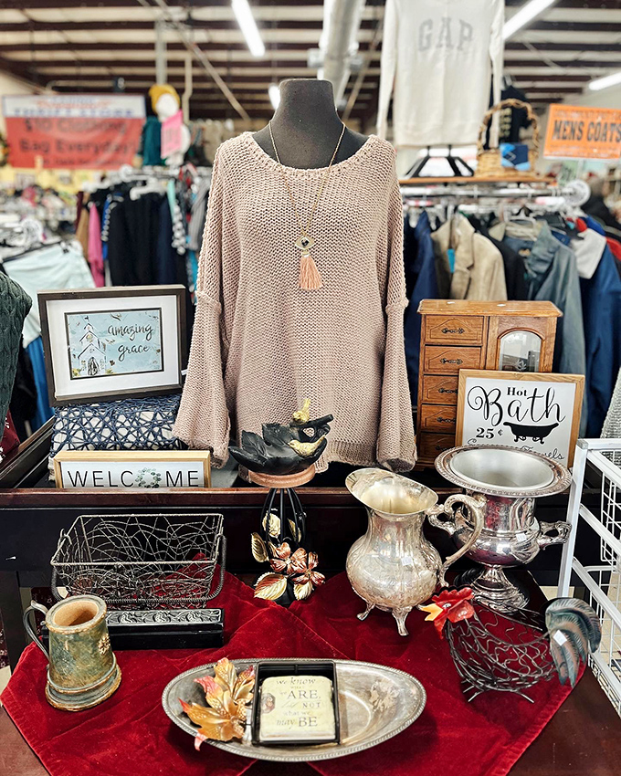 Curated chaos at its finest. This artful display marries vintage silver, inspirational signs, and cozy sweaters into a perfect thrift store vignette.