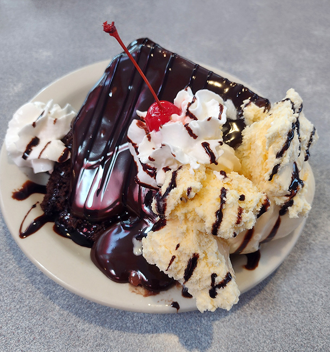 Hot fudge cascading over cake like chocolate lava, with whipped cream islands that deserve their own vacation postcards.