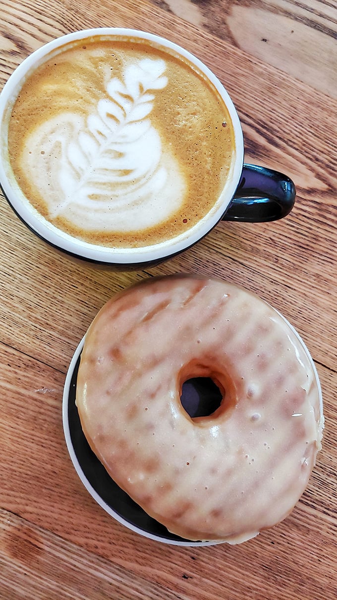 The perfect pairing: a beautifully crafted latte with leaf design alongside a glazed donut that glistens with promise.