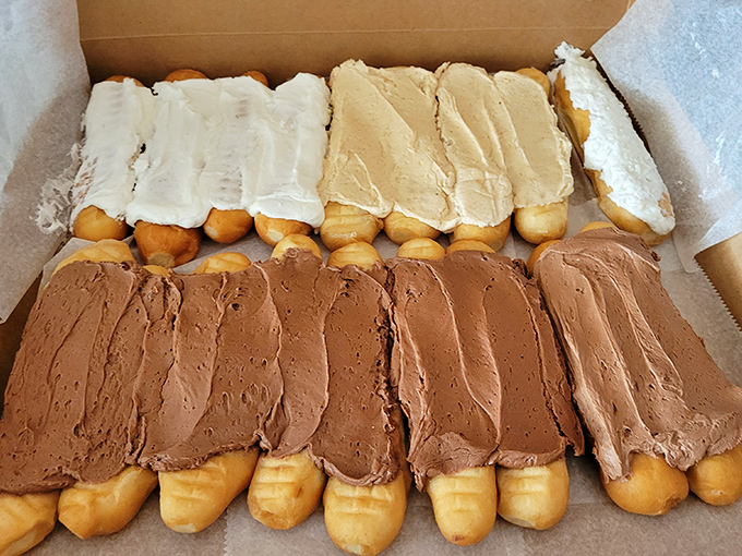 A box of frosted Long Johns lined up like sweet soldiers. The chocolate ones aren't just topped—they're lavishly dressed for a formal sugar ball.