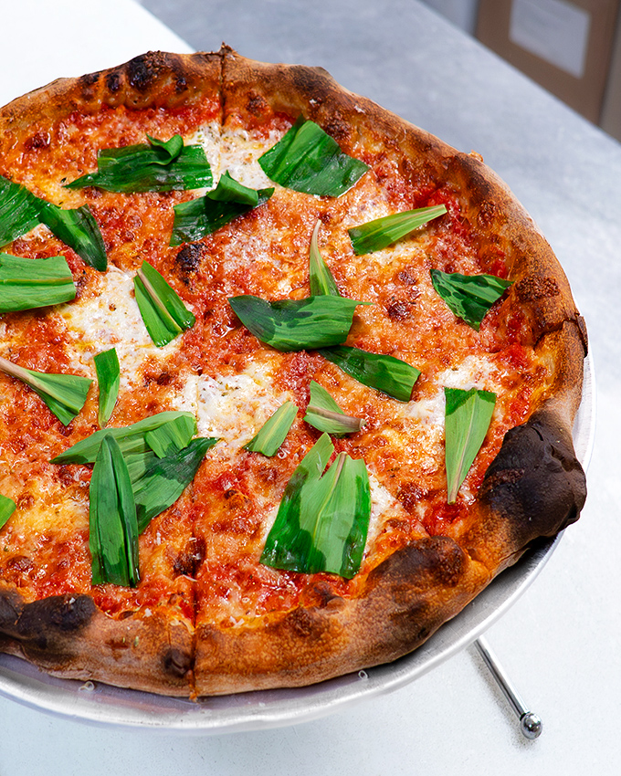 Fresh greens atop that perfect leopard-spotted crust. Like spring decided to take a delicious vacation on your pizza.