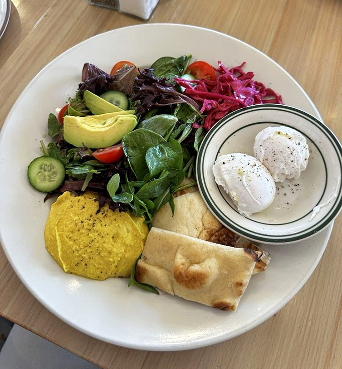 The Mediterranean breakfast plate—where poached eggs, fresh vegetables, and hummus prove that breakfast doesn't always need maple syrup to be magnificent.