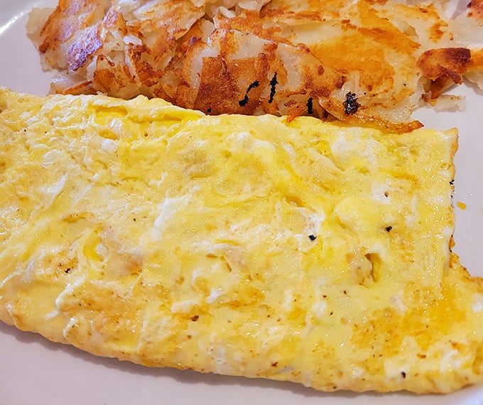 An omelet so fluffy it practically hovers above the plate, keeping company with hashbrowns that have achieved that mythical balance of crispy exterior and tender interior.