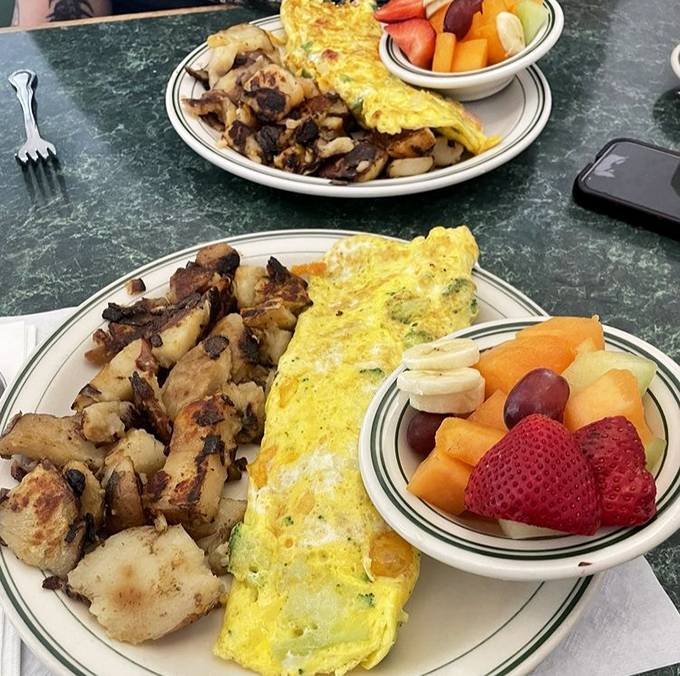 Two plates showcasing the art of the perfect omelet &ndash; folded like a letter containing good news, alongside home fries that deserve their own fan club.