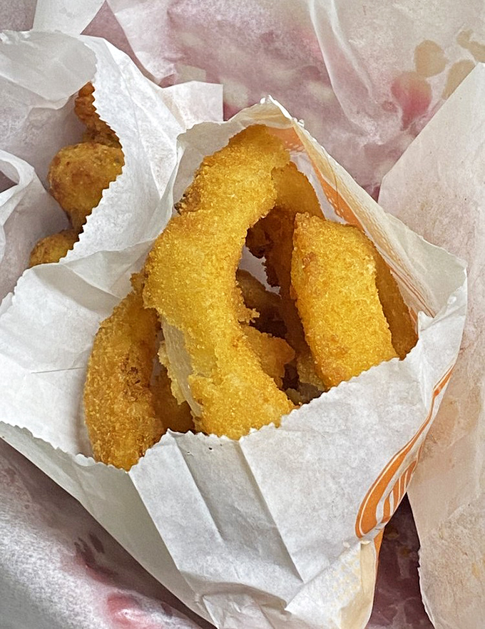 Golden-fried onion rings nestled in paper like precious artifacts. These crispy halos aren't just side dishes&mdash;they're the main event masquerading as supporting characters.