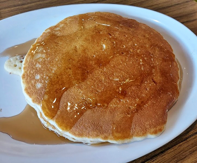 The pancake that launched a thousand return visits. Golden-brown, perfectly round, and waiting for that slow maple syrup pour that makes life worth living.