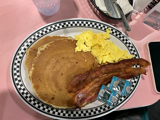 The breakfast trinity: golden pancakes, perfectly scrambled eggs, and bacon so crisp it practically snaps a salute when you pick it up.