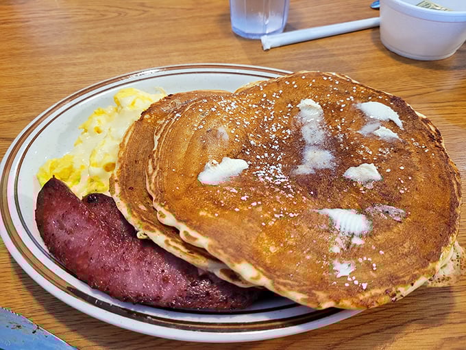 Golden-brown pancakes with melting butter pockets, powdered sugar, and a side of ham that means business. Breakfast architecture at its most satisfying.