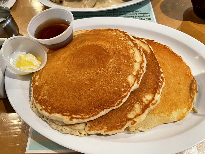 Pancakes so perfectly golden they belong in Fort Knox. These fluffy discs of joy arrive with butter slowly melting into their warm embrace.