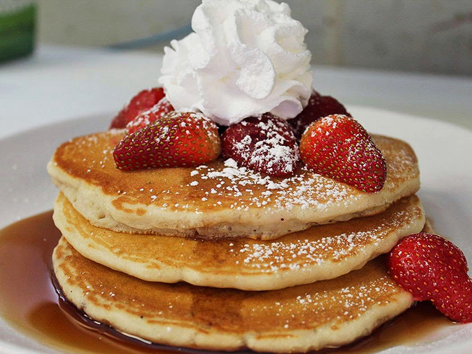 Pancakes stacked higher than your weekend expectations, crowned with fresh strawberries and a dollop of whipped cream that means business.