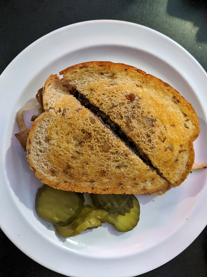 The humble patty melt: bread toasted to golden perfection, embracing beef and melted cheese with pickle spears standing guard nearby.