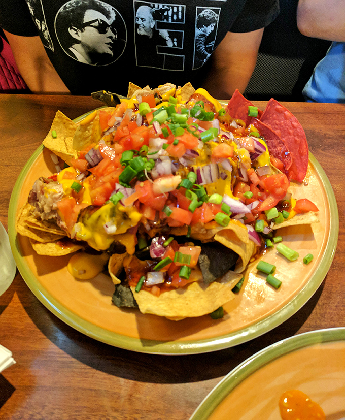 These nachos aren't just topped, they're architecturally engineered – a mountain of pulled pork, cheese, and fresh veggies that demands to be conquered.