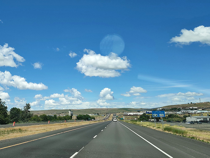 The road to Pendleton unfolds beneath endless blue skies, where puffy clouds float like thoughts above the golden Eastern Oregon landscape.