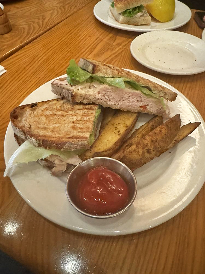 A sandwich that understands the importance of balance—crispy bread, tender turkey, fresh greens, and those potato wedges that deserve their own fan club.