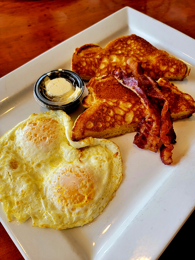 The breakfast trinity: golden French toast, perfectly cooked eggs, and bacon that's achieved that magical balance between crisp and chewy.