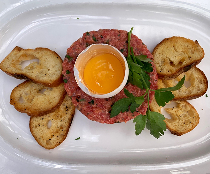 Steak tartare presented with reverence &ndash; hand-chopped beef with the perfect egg yolk crown, surrounded by crisp crostini soldiers waiting for their marching orders.