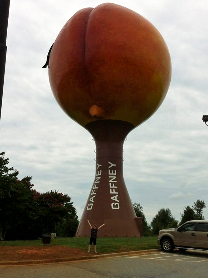 A visitor strikes the classic "I conquered the Peachoid" pose, demonstrating the proper way to document your pilgrimage to fruit tower greatness.