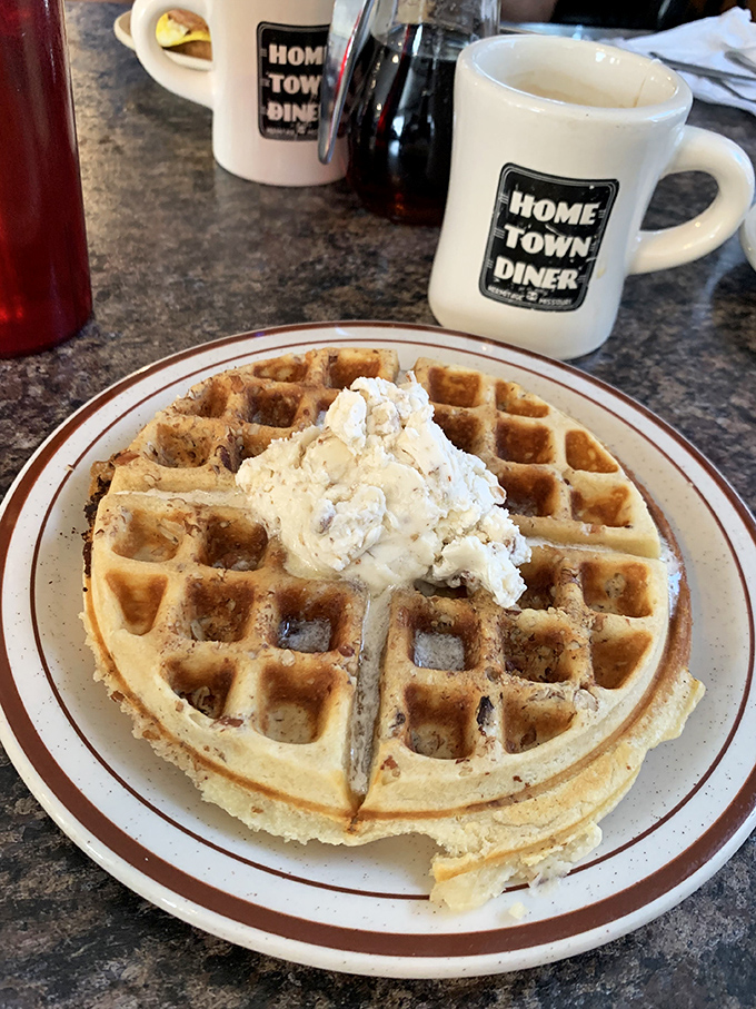 A perfect waffle crowned with a dollop of butter &ndash; served on the diner's signature plate with their branded mug standing guard nearby.