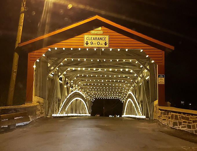 By night, the bridge transforms into a magical passage, string lights illuminating its wooden skeleton like stars captured in an architectural constellation.