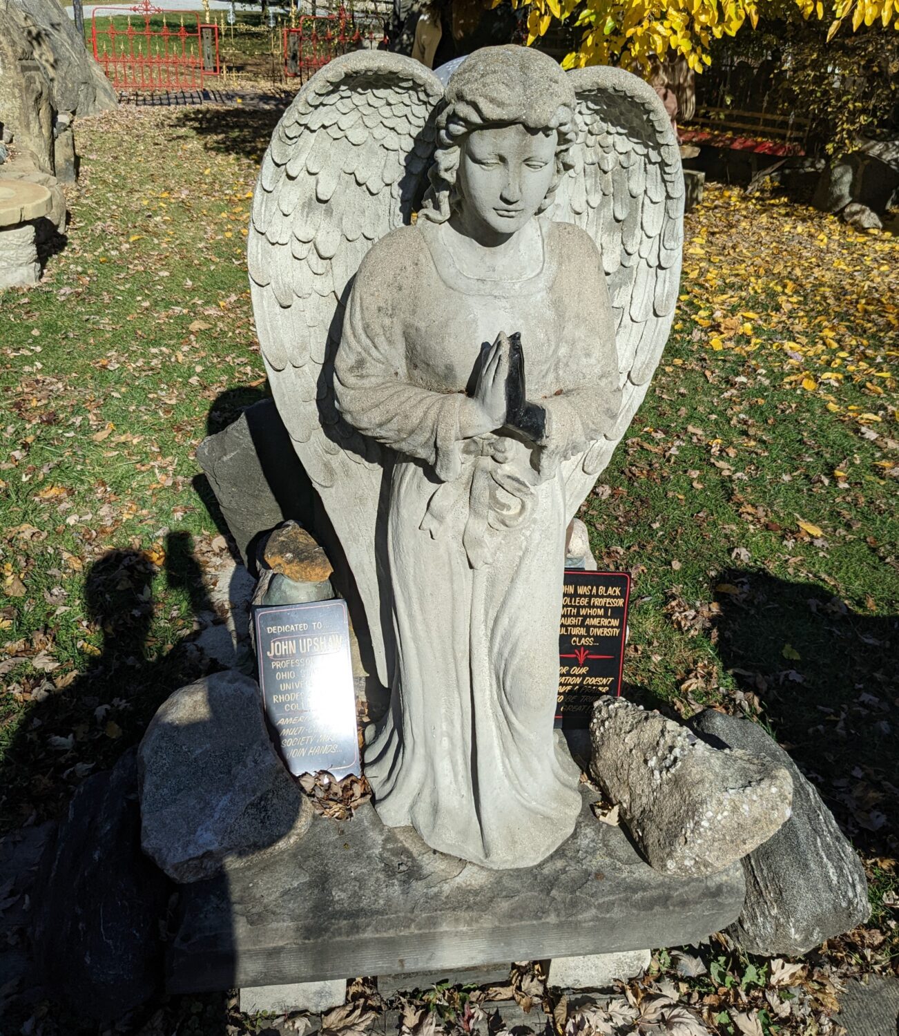 A serene angel stands guard among autumn leaves. In this garden of stone, even concrete figures seem to radiate peaceful energy.