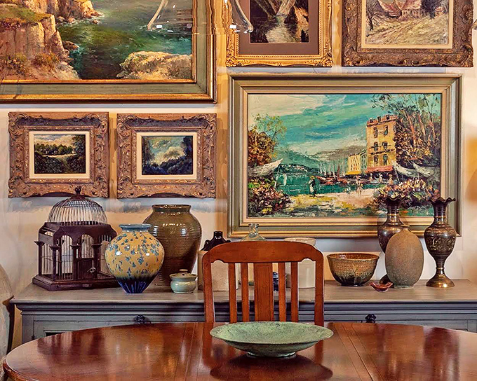 The art wall creates a salon-style gathering where landscapes, seascapes, and still lifes mingle like guests at a particularly cultured cocktail party.