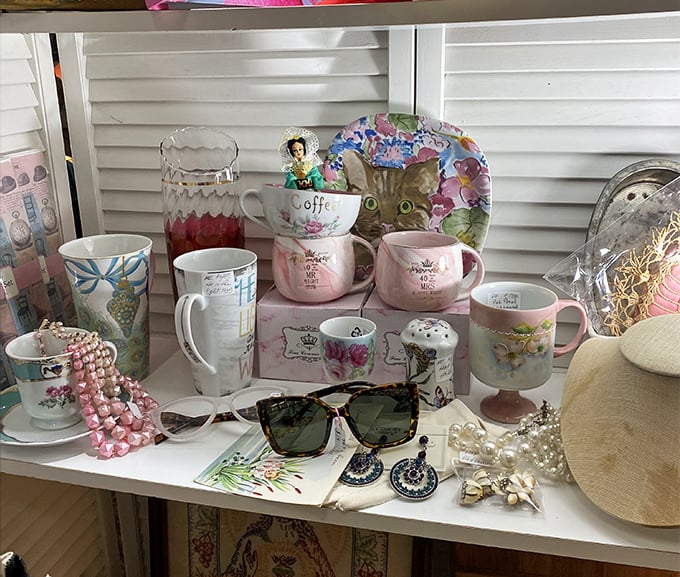 Delicate teacups and sassy mugs share shelf space like old friends at a reunion, pink pearls and vintage sunglasses completing the tableau.