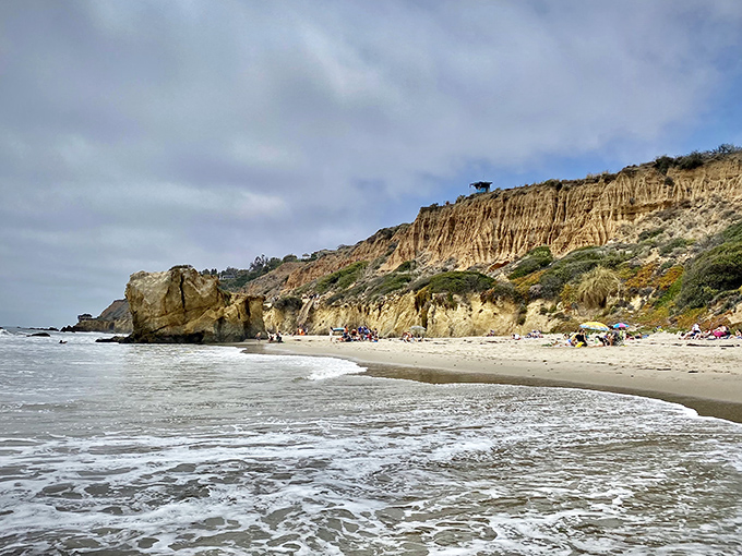 The golden cliffs stand guard over beachgoers like ancient sentinels. Even on cloudy days, this stretch of coast glows with California magic.