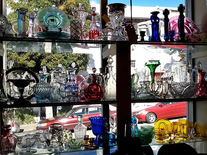 Sunlight streams through colored glass, creating a rainbow effect that no Instagram filter could ever replicate. Vintage glassware becomes art in this display.