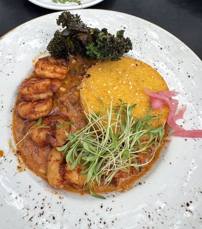Shrimp and grits reimagined: a golden grit cake island in a sea of savory sauce with plump shrimp standing guard.