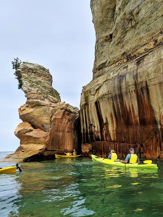 Kayakers paddle through a natural art gallery where mineral-stained cliffs create a canvas millions of years in the making.