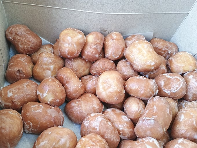 Fresh glazed donuts piled like golden treasure in boxes that barely contain their magnificent presence.