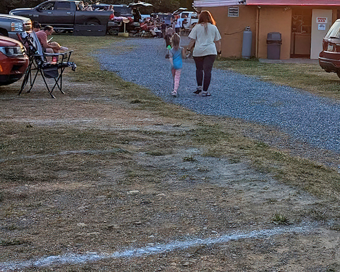 Families making memories between cars and concessions. The pre-show ritual of finding the perfect spot for your lawn chair is sacred drive-in choreography.