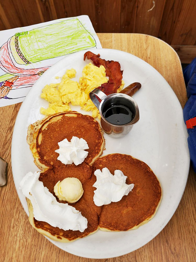 Pancakes with whipped cream smiles, served alongside golden eggs and bacon. Even the children's artwork approves of this masterpiece.