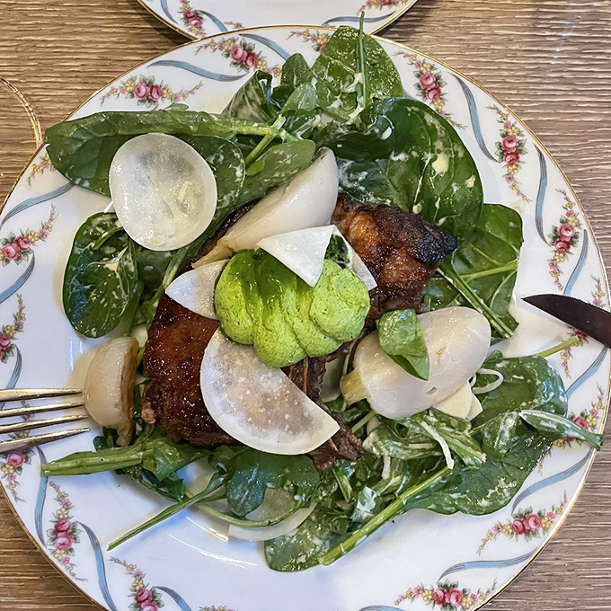A pork chop nestled on spinach with turnips and avocado—proof that simple ingredients become extraordinary in skilled hands.