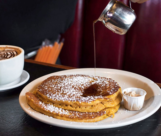 Syrup cascades over golden pancakes like a sweet waterfall, creating that perfect moment between presentation and delicious destruction.