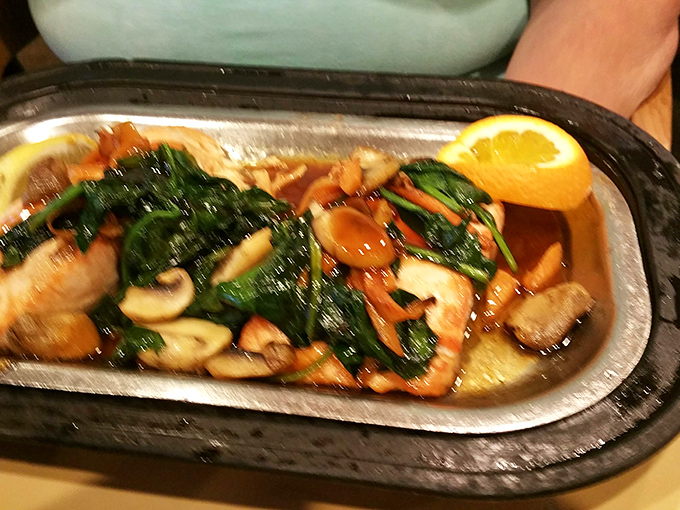 The salmon arrives sizzling on its metal platter, surrounded by spinach and mushrooms like a seafood celebrity with its entourage.
