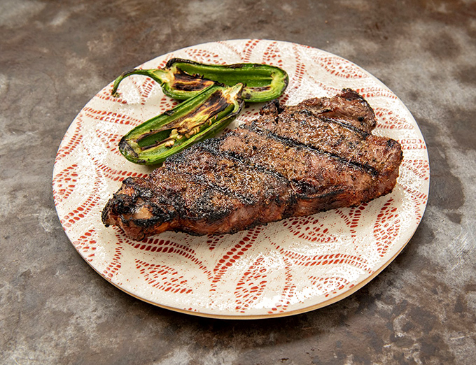 A steak and grilled jalape&ntilde;os on a decorative plate &ndash; proof that in Texas, even fancy dishware knows its supporting role.