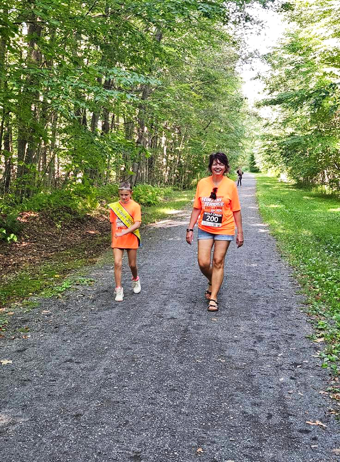 Lush green canopies create natural tunnels along Mount Jewett's trails, where hikers in bright orange shirts add splashes of color to the woodland palette.