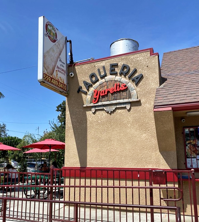 The red fence and outdoor seating create the perfect California taco experience under sunny skies and swaying palm trees.