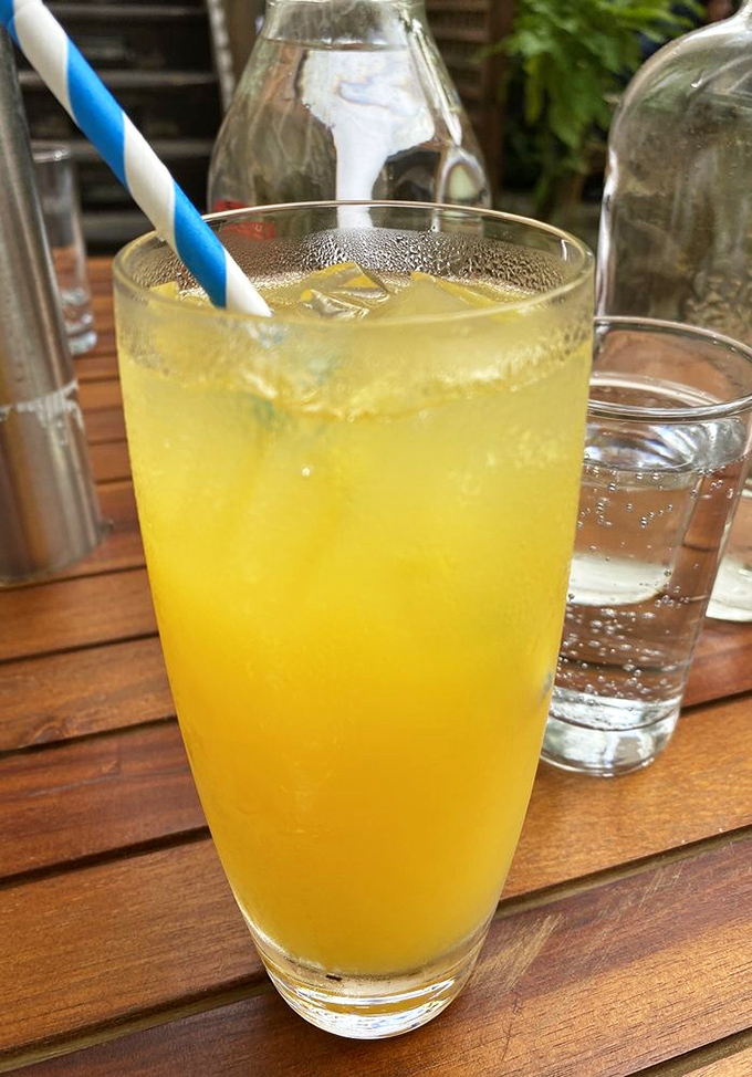 That refreshing yellow drink, likely house-made lemonade or a citrus cocktail, offering liquid sunshine in a glass with a jaunty straw.