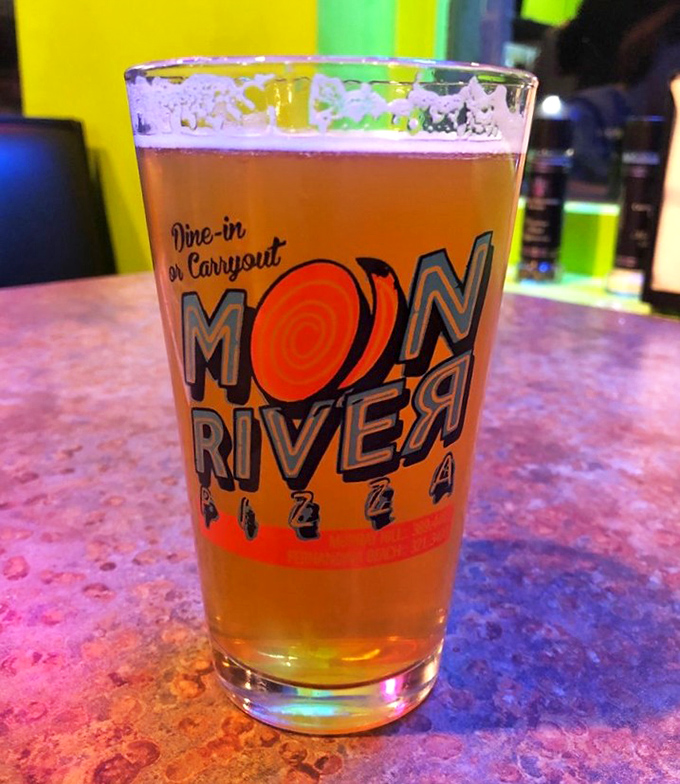 A cold craft beer in a branded glass—the perfect companion for pizza exploration. The amber liquid promises refreshment between bites.