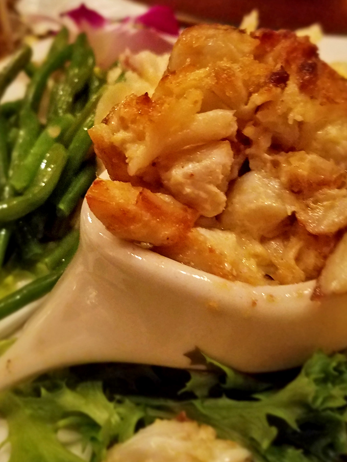 Seafood architecture at its finest: delicate crab imperial nestled in a shell, flanked by vibrant green beans that add color to the masterpiece.