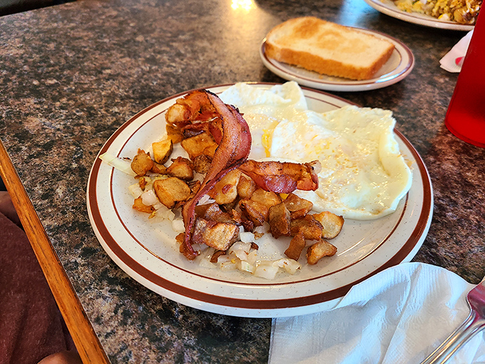 Sunny-side eggs, crispy home fries, and bacon arranged with the casual precision that comes from decades of breakfast-making expertise.