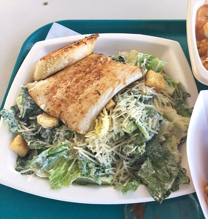 A perfectly grilled mahi fillet perches atop a Caesar salad like a crown jewel, proving that sometimes the simplest preparations are the most magnificent.