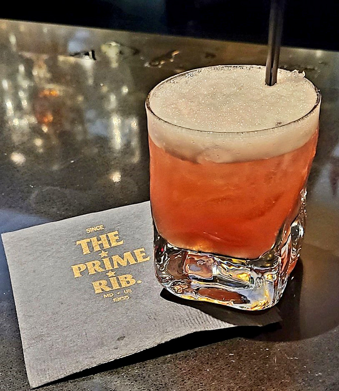 A proper cocktail demands proper glassware. This Caribbean punch, amber-hued and frothy-topped, sits regally on its napkin throne, waiting to transport you to island time.