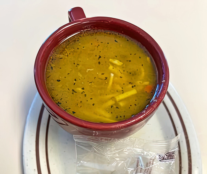 Chicken noodle soup that looks like someone's grandmother made it with love, served in a mug that says, "Take your time, we're not fancy here."