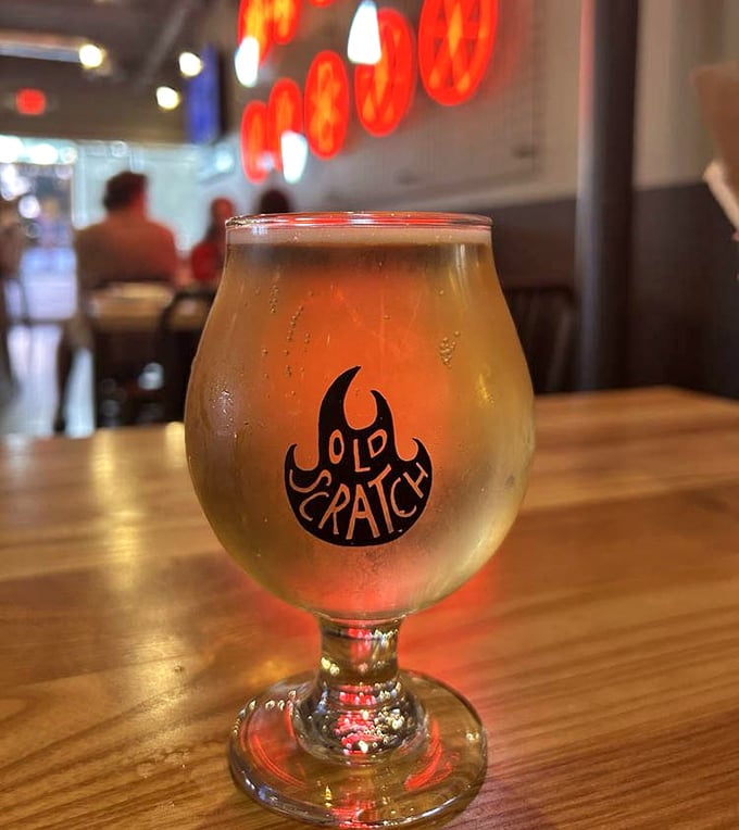A golden glass of craft beer sporting the Old Scratch logo&mdash;because what pairs better with wood-fired pizza than a perfectly poured pint?