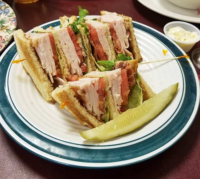 A club sandwich stacked higher than your weekend to-do list, with a pickle standing guard against mundane lunches.