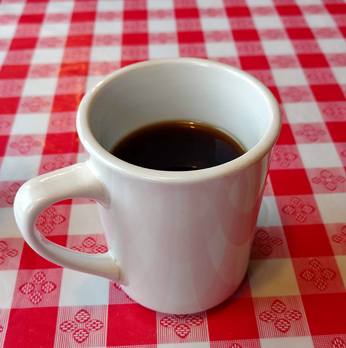 Simple black coffee in a white mug on a red-checkered tablecloth—Norman Rockwell couldn't have painted a more quintessentially American diner moment.