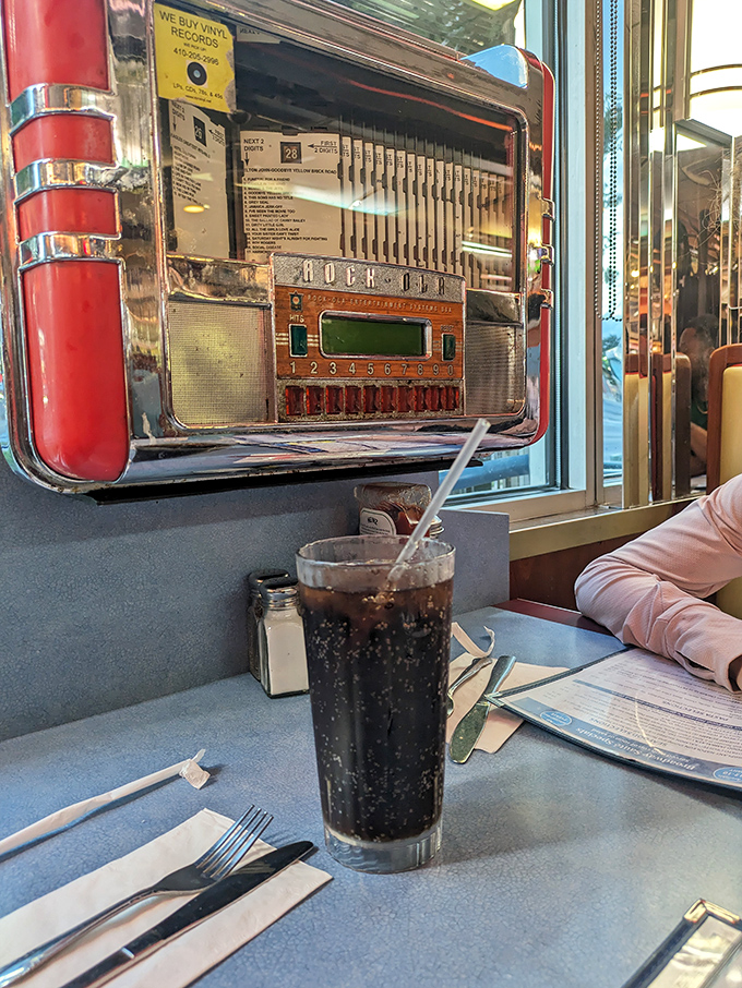 That classic diner soda moment: ice-cold cola in a tall glass, with a vintage jukebox promising tunes as refreshing as your drink.
